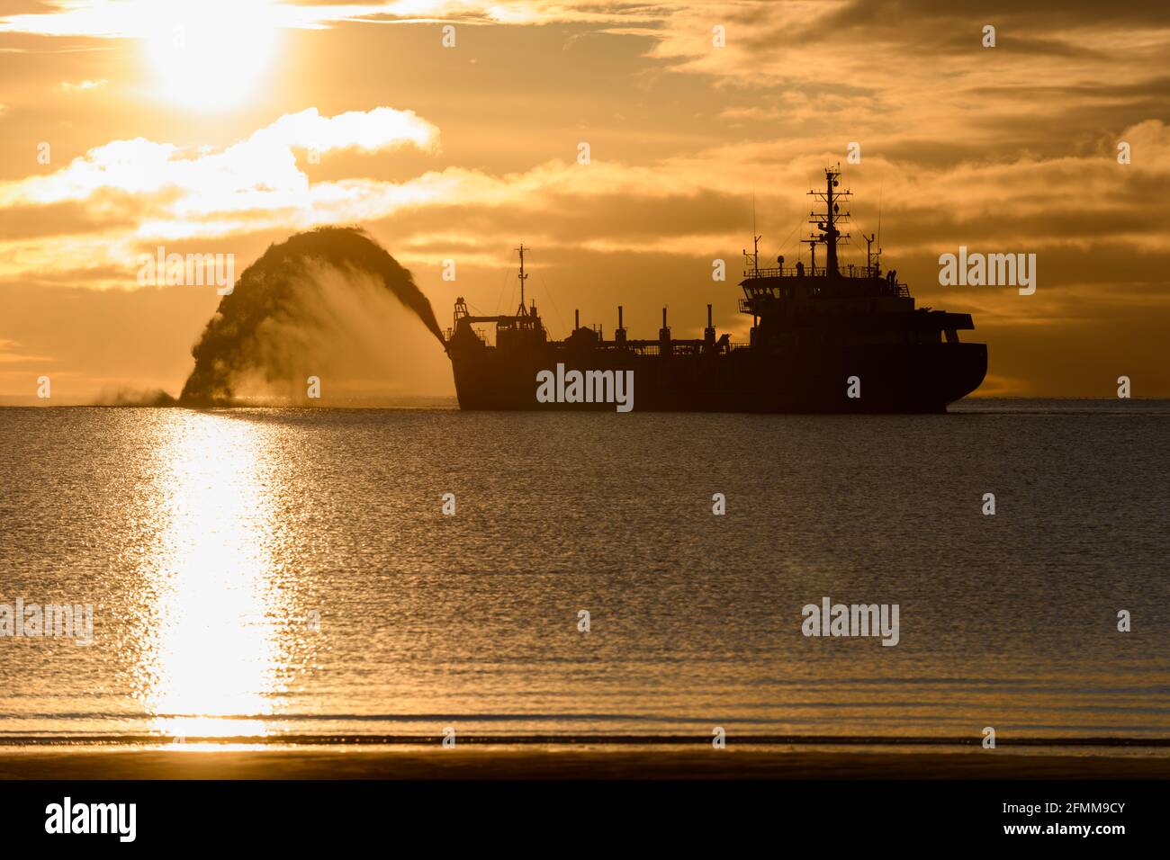 Vessel engaged in dredging at sunset time. Hopper dredger working at ...