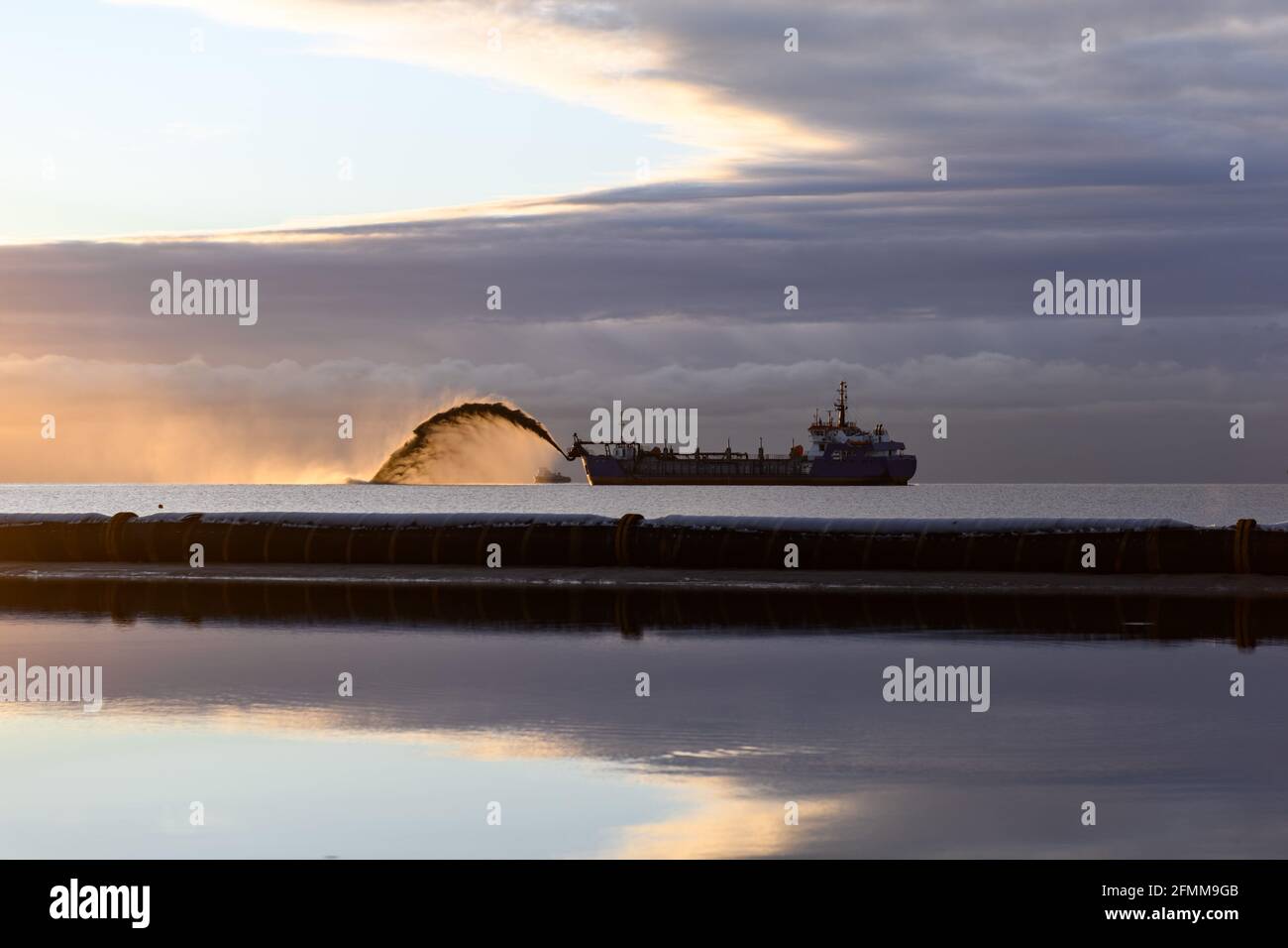 Vessel engaged in dredging at sunset time. Hopper dredger working at ...