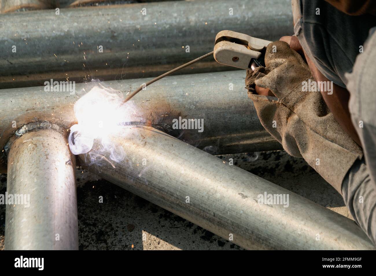 A welder is sitting on a steel roof frame and is welding steel pipes ...