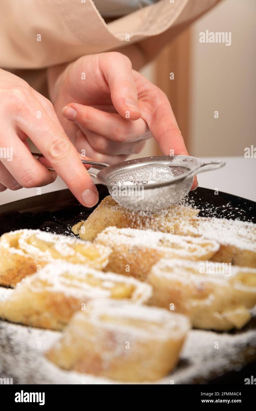 Chef sprinkles icing sugar on the apple roll. Strudel feed. Vertical ...