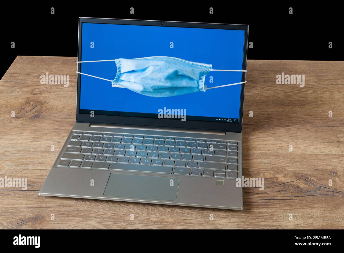 Protective face mask on blue laptop screen, wooden desk with black ...