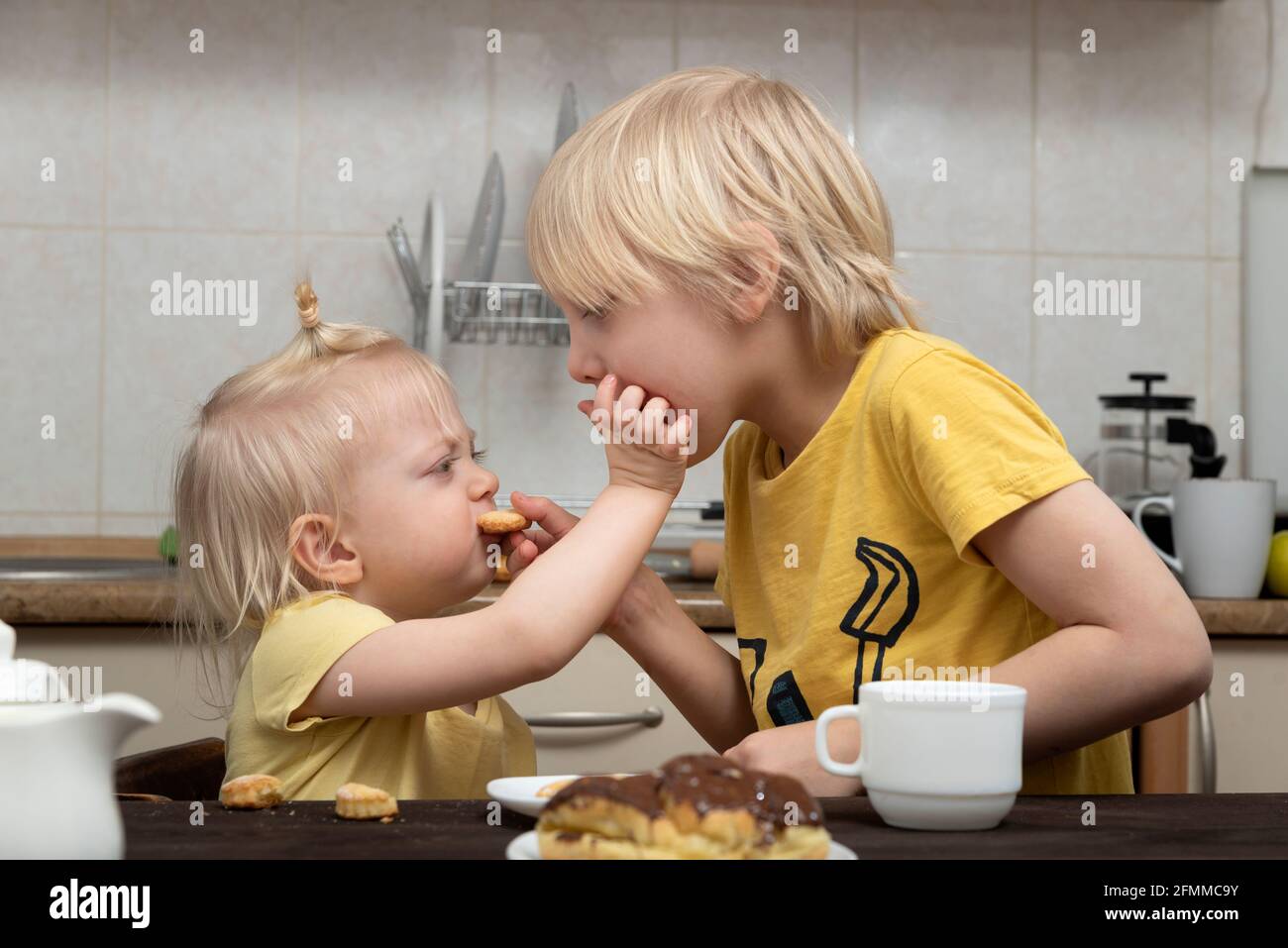 Blond brother and sister feed each other cookies. Siblings Stock Photo ...
