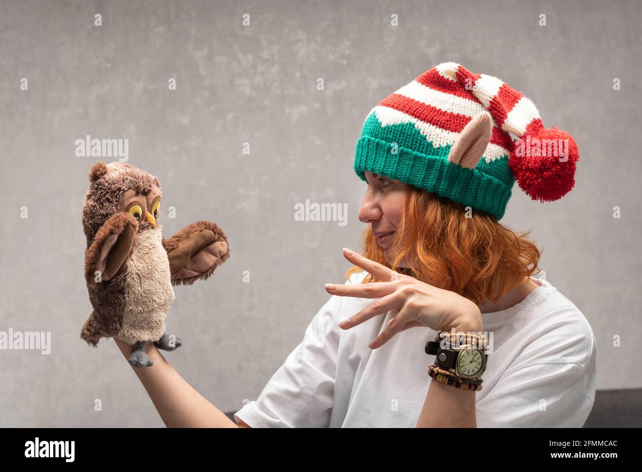 Red-haired girl in an elf hat talking with toy. Funny girl and toy owl ...