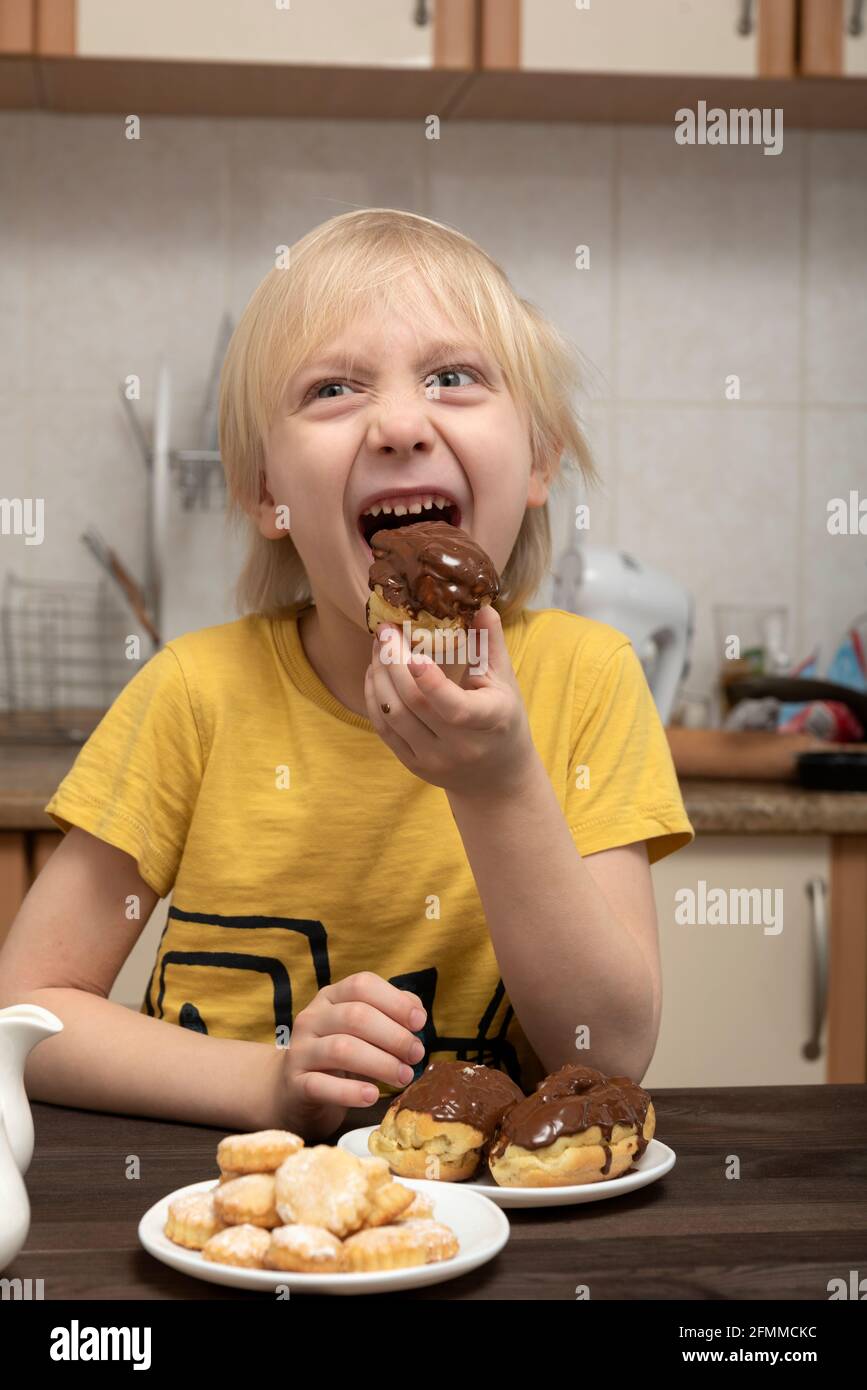 Happy blond boy is eating cake. Child eats an eclair. Vertical frame ...