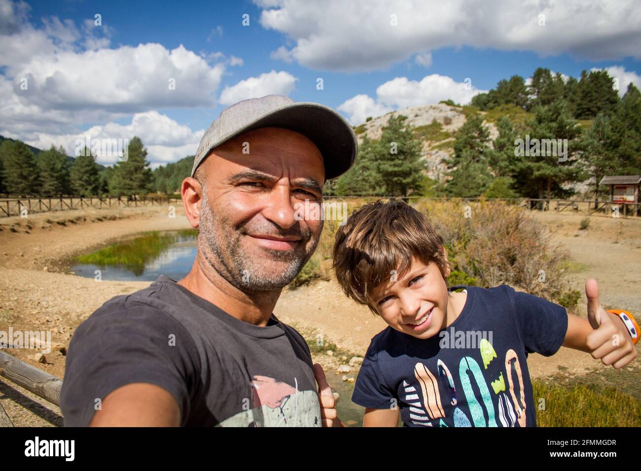 Happy Spanish father and son taking a selfie in a park under a bright ...