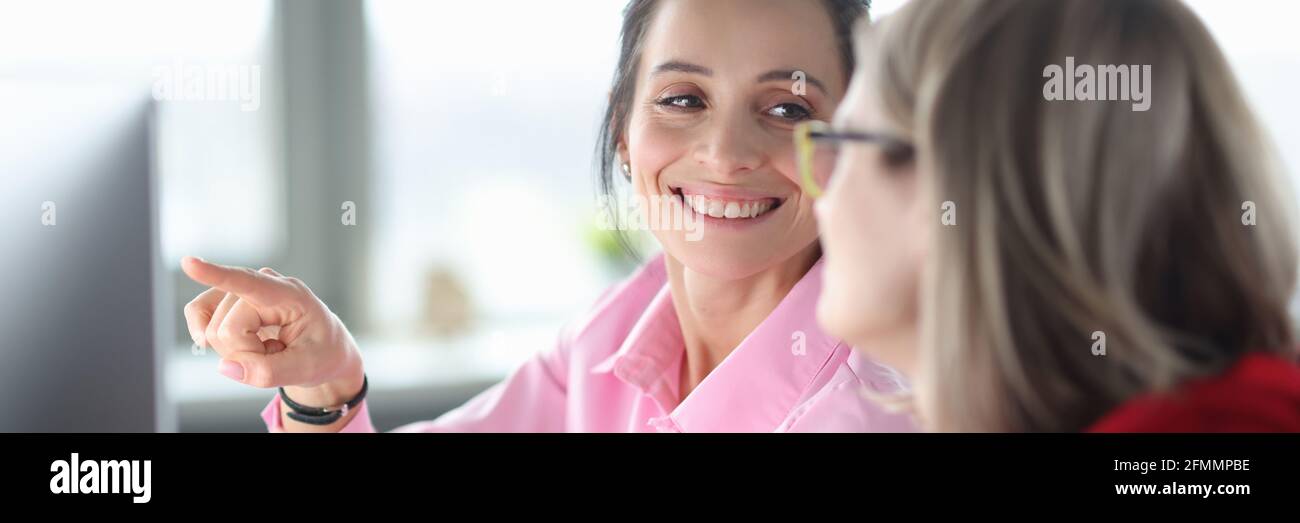 Two smiling women at work desk point to the monitor Stock Photo - Alamy