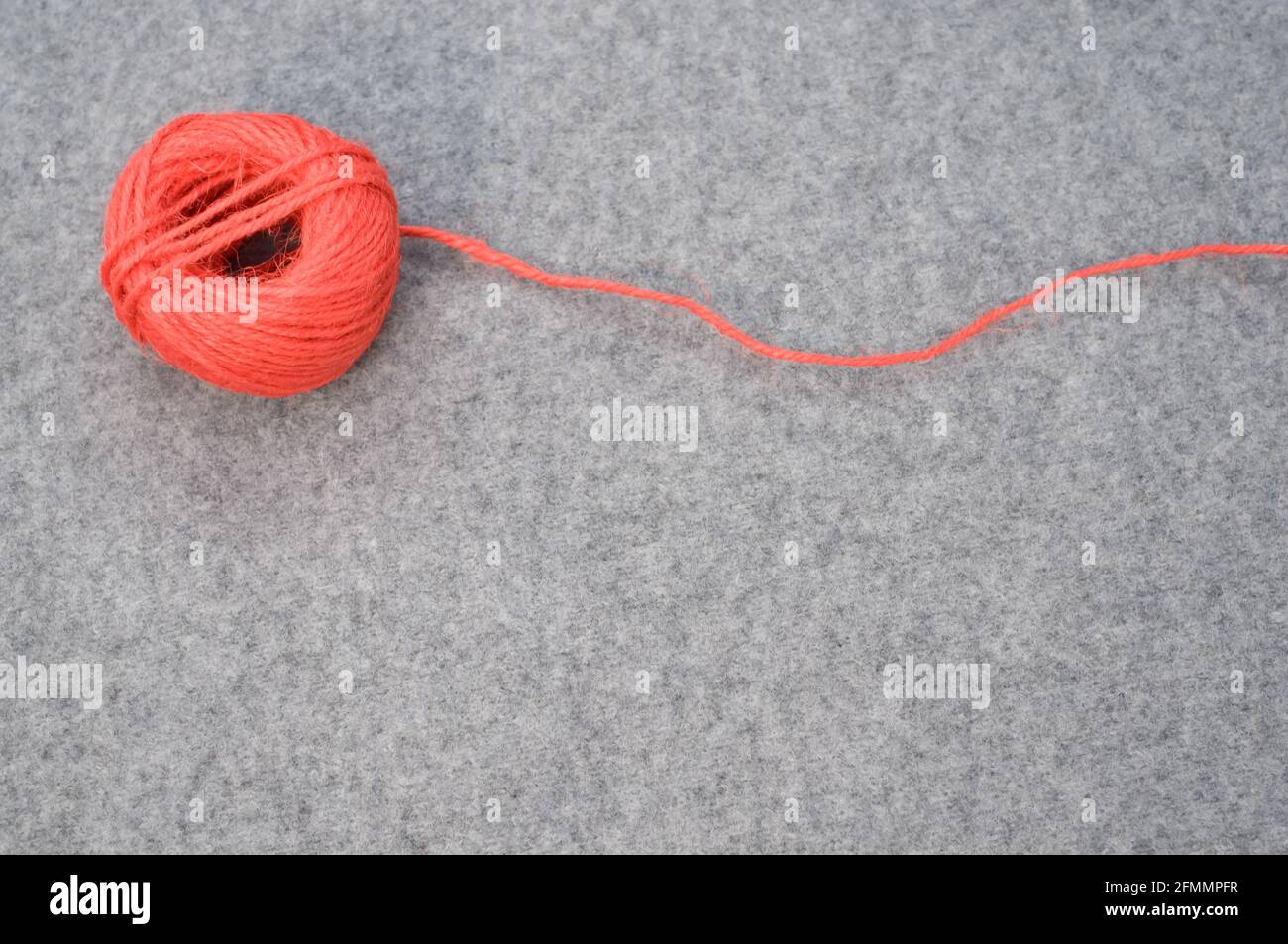 Red coil of yarn on a gray background with a loose string and copy ...