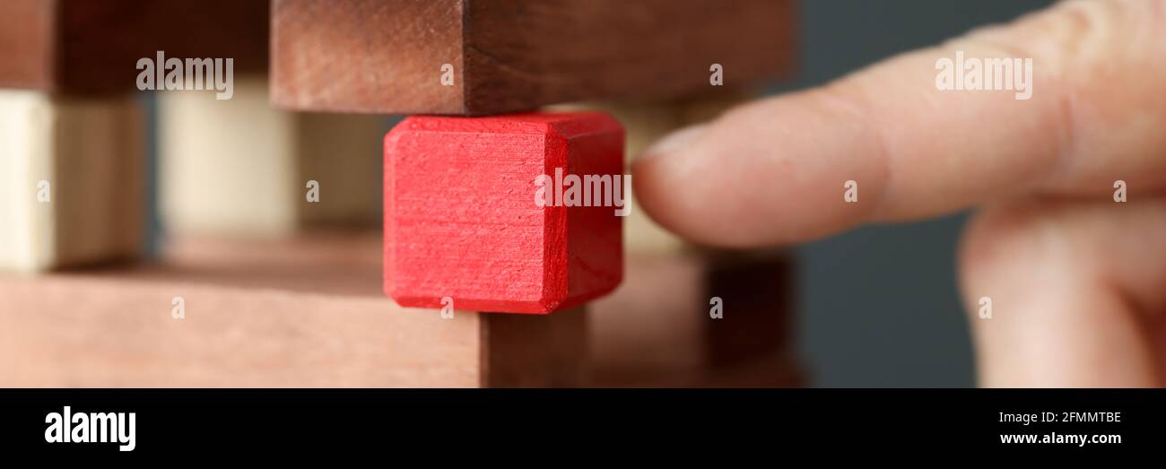 Wooden tower made of wooden brown cubes from which red cube is taken ...