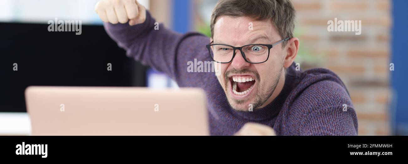 Angry man with glasses waves his fist at laptop monitor Stock Photo - Alamy