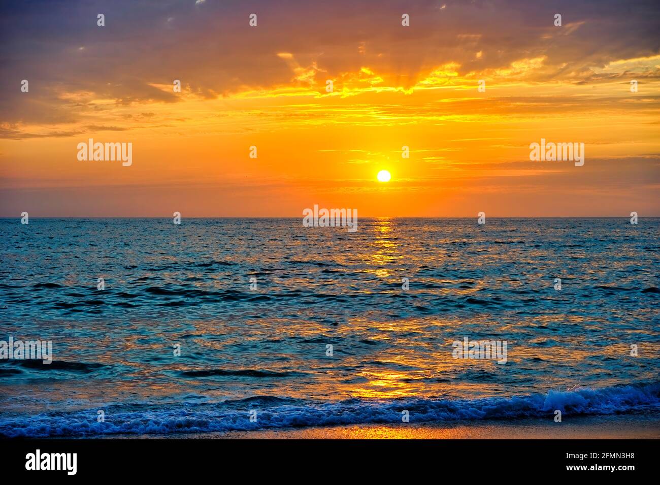 A Colorful Ocean Sunset Sky as a Gentle Wave Rolls to Shore Stock Photo ...