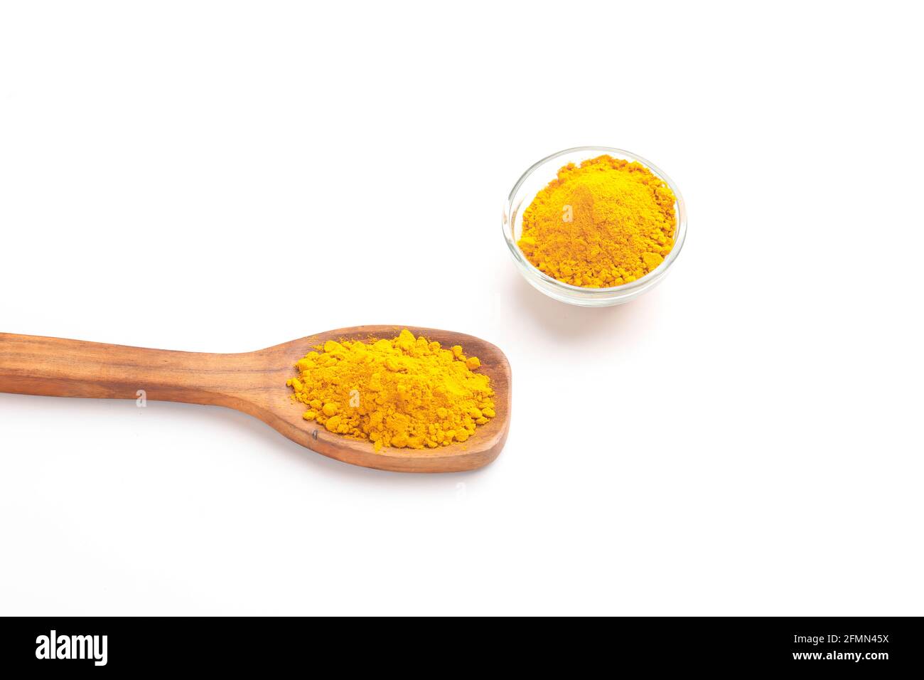 Turmeric powder in wooden spoon and glass bowl on white background ...