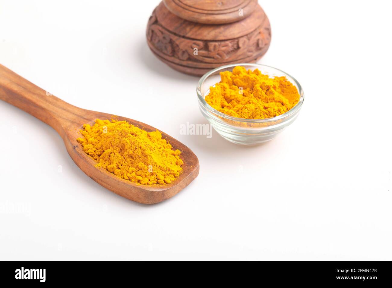 Turmeric powder in wooden spoon and glass bowl on white background ...