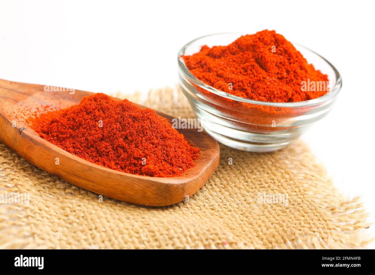 close view of red chilli powder in wooden spoon on white background ...