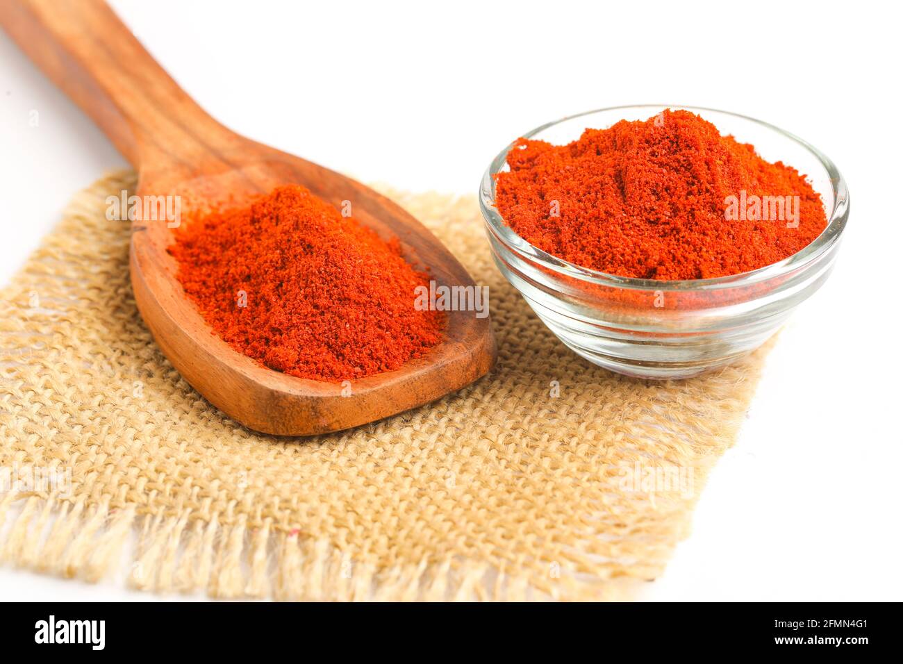 close view of red chilli powder in wooden spoon on white background ...