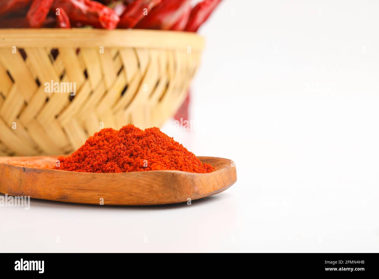 close view of red chilli powder in wooden spoon on white background ...