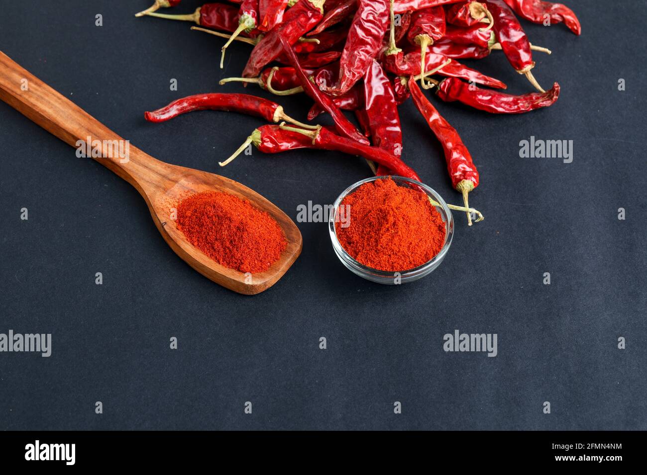 Dried red chilli and powder in glass bowl and wooden spoon on dark ...