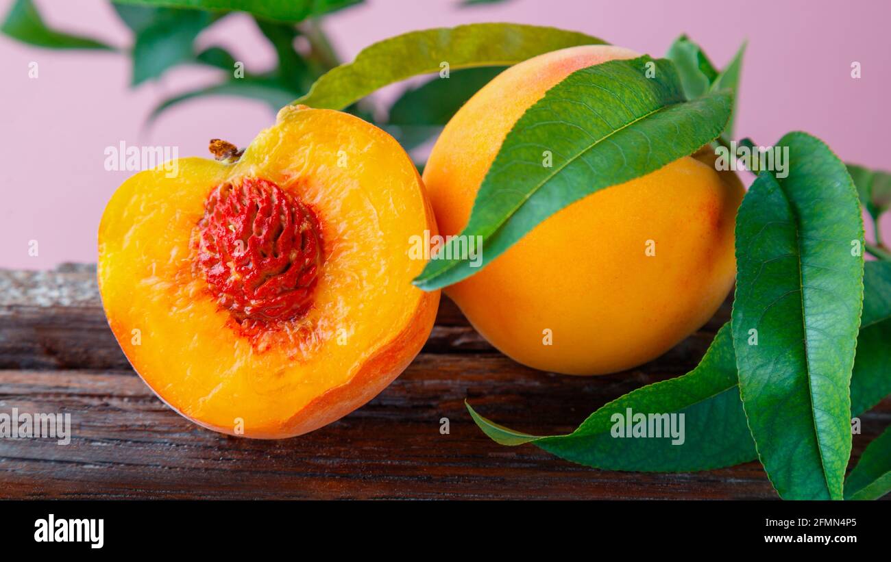 Peach in halves with bone. Peaches with leaves on wooden board. Ripe ...