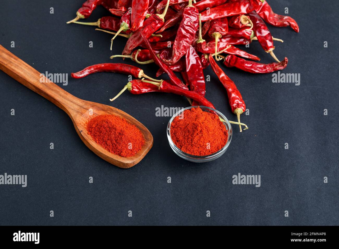 Dried red chilli and powder in glass bowl and wooden spoon on dark ...