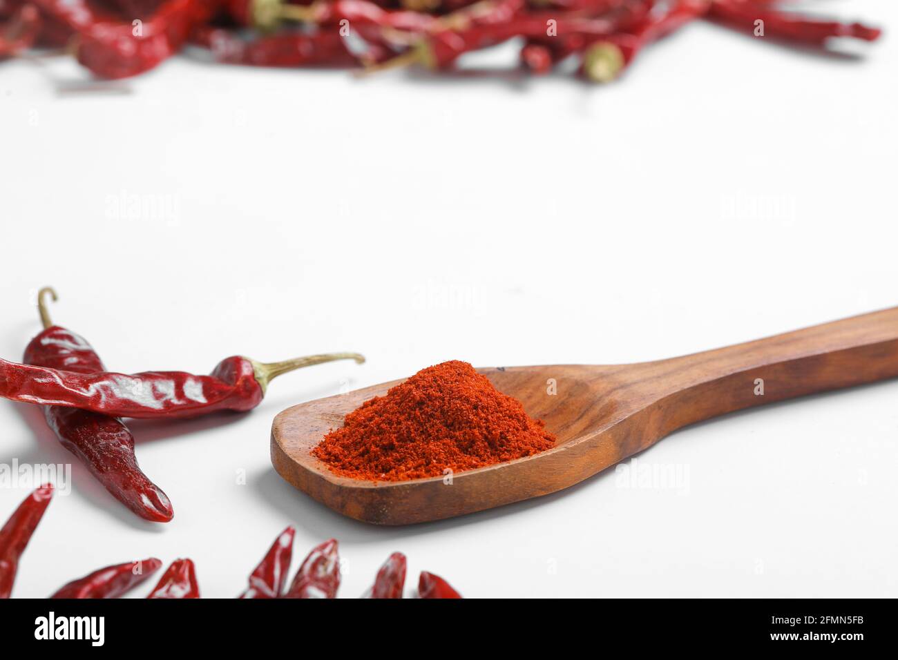 Chilli powder in wooden spoon with dry red chilly on white background ...