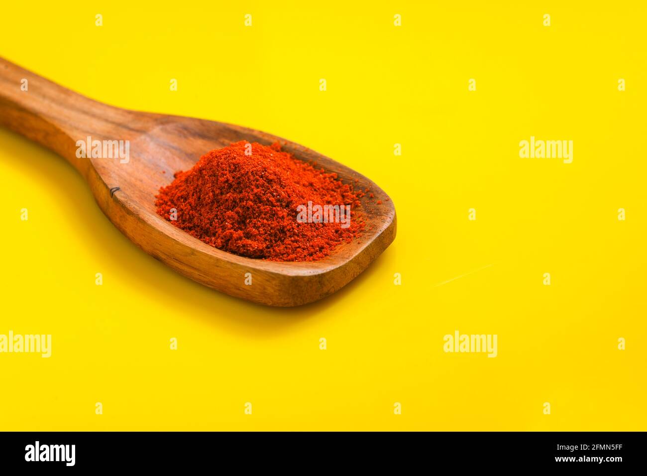 Chilli powder in wooden spoon with dry red chilly on yellow background ...