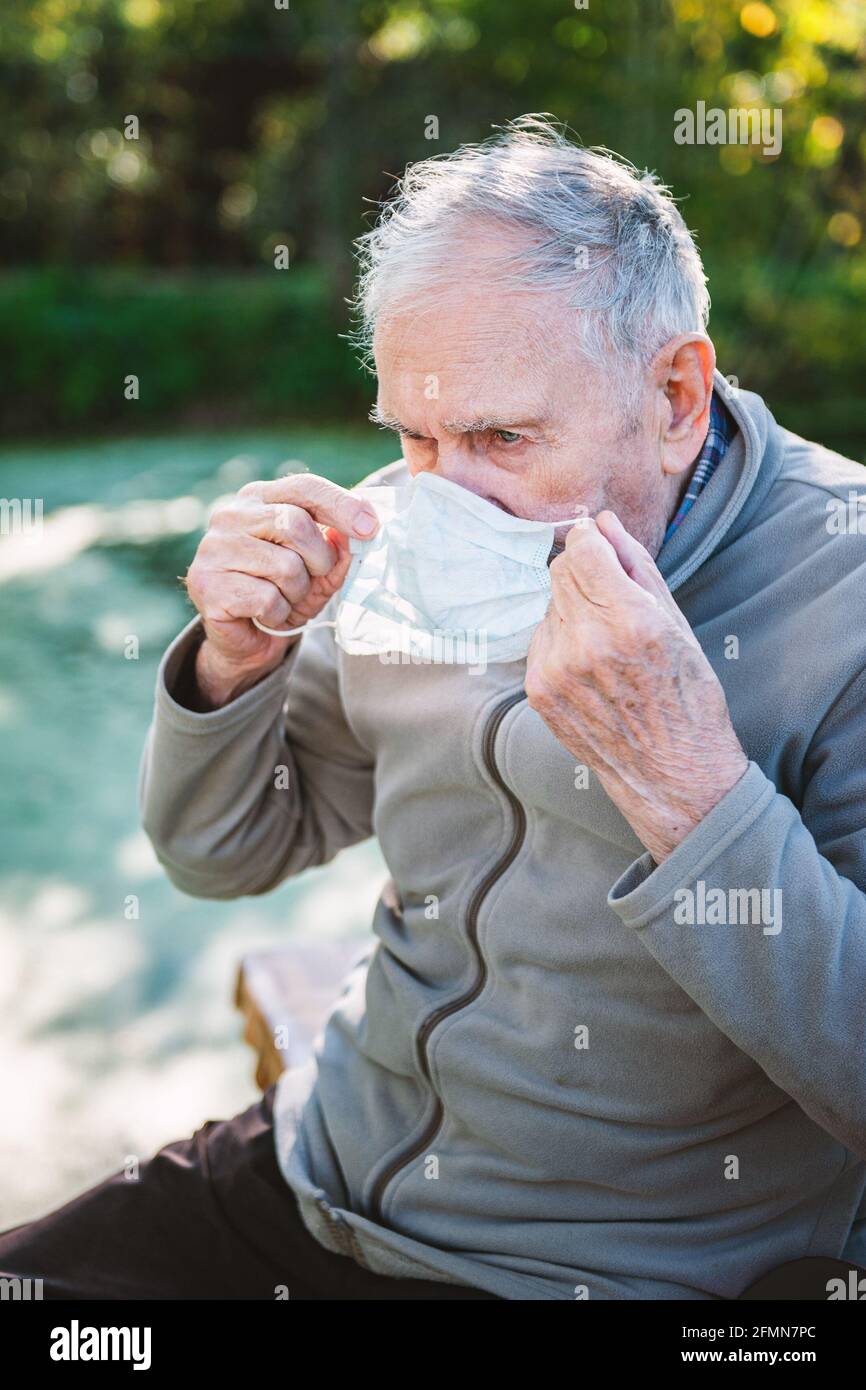 An old 87-year-old man puts on a mask while sitting outside. Protection ...