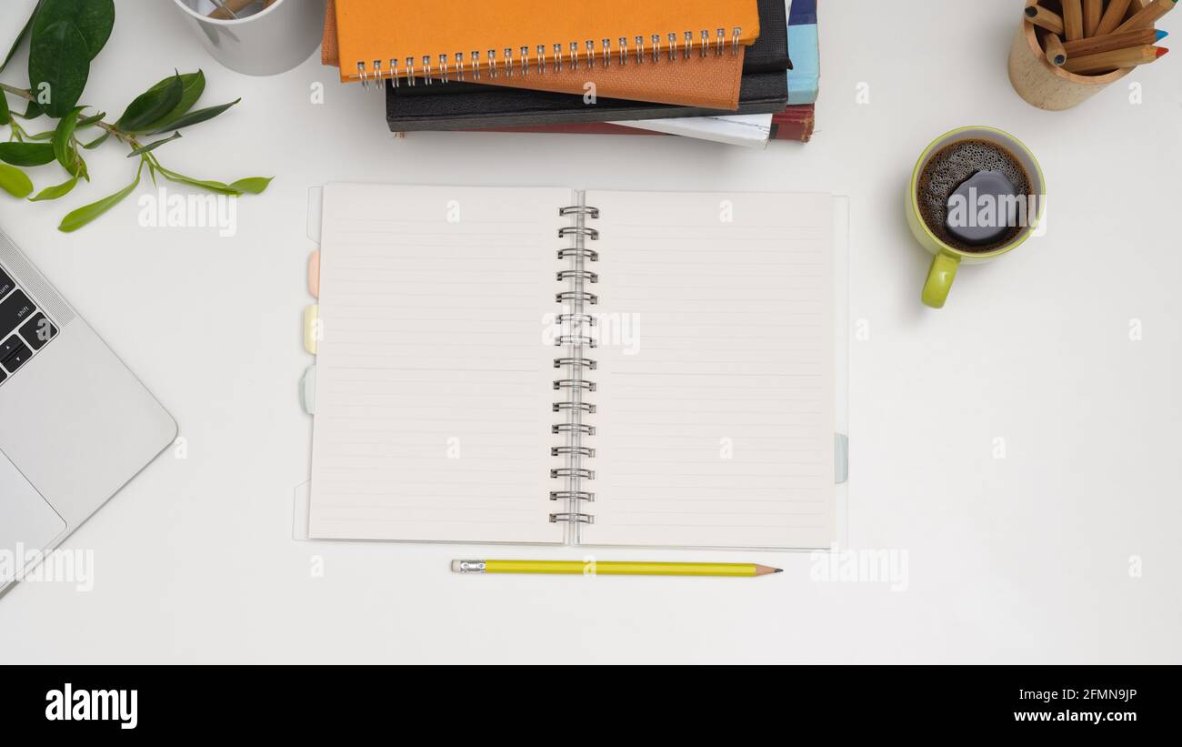Top view of study table with opened blank notebook, laptop, stack of ...