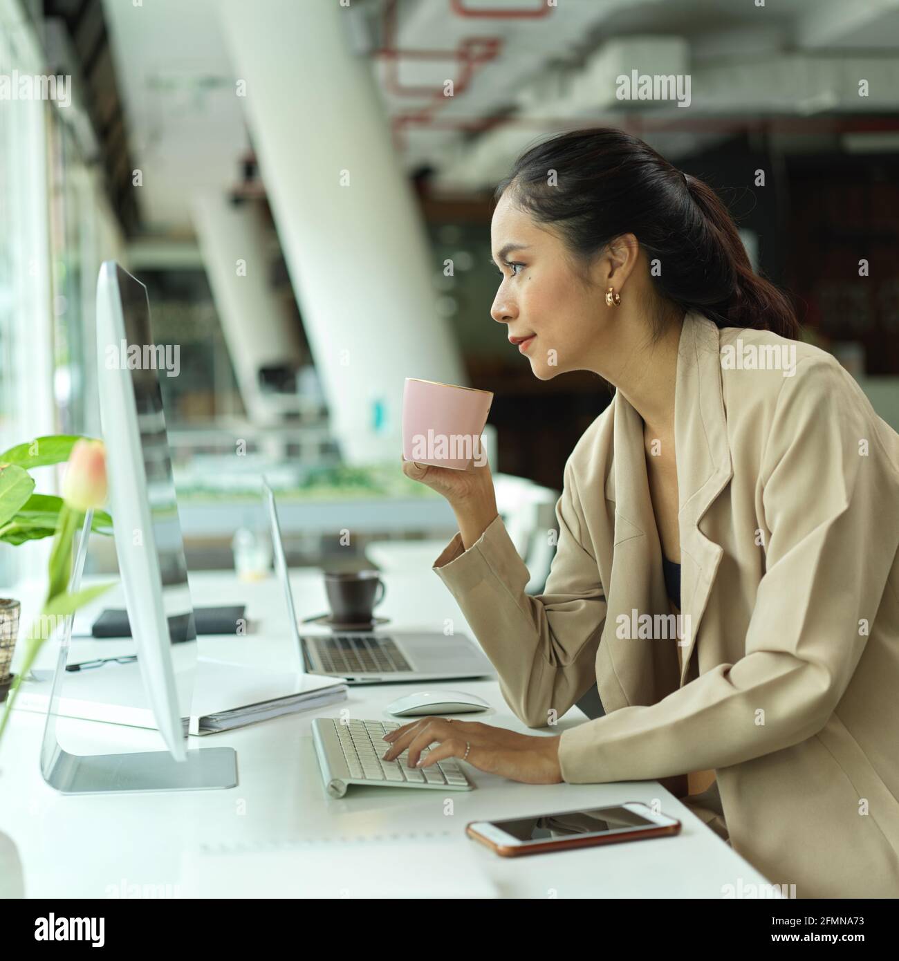 Side view of female office worker drinking coffee while working on ...