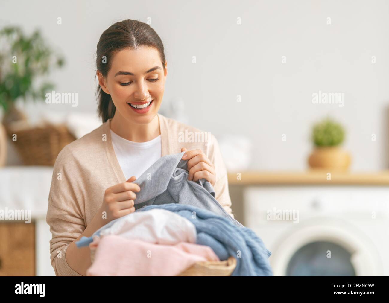 Beautiful young woman is smiling while doing laundry at home Stock ...