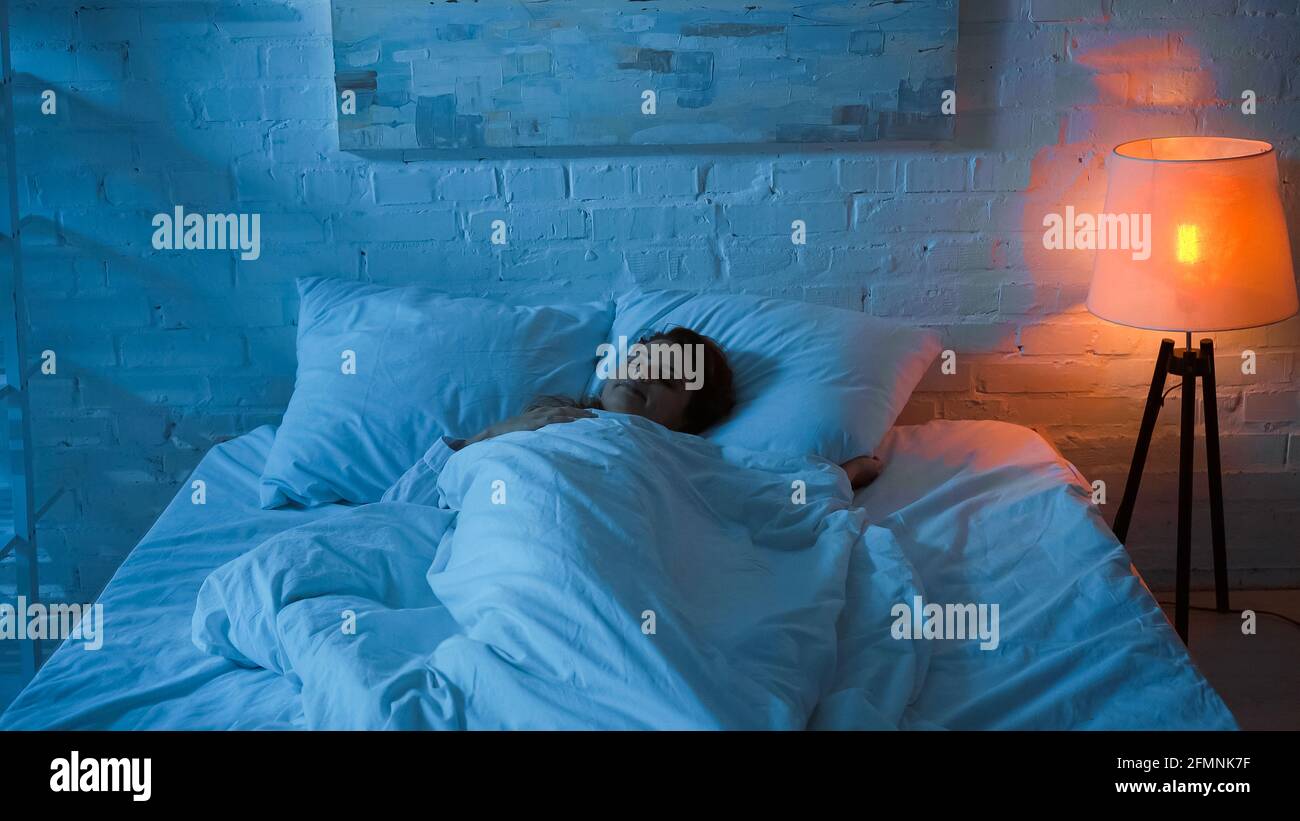 Woman sleeping on bed near floor lamp in bedroom Stock Photo - Alamy