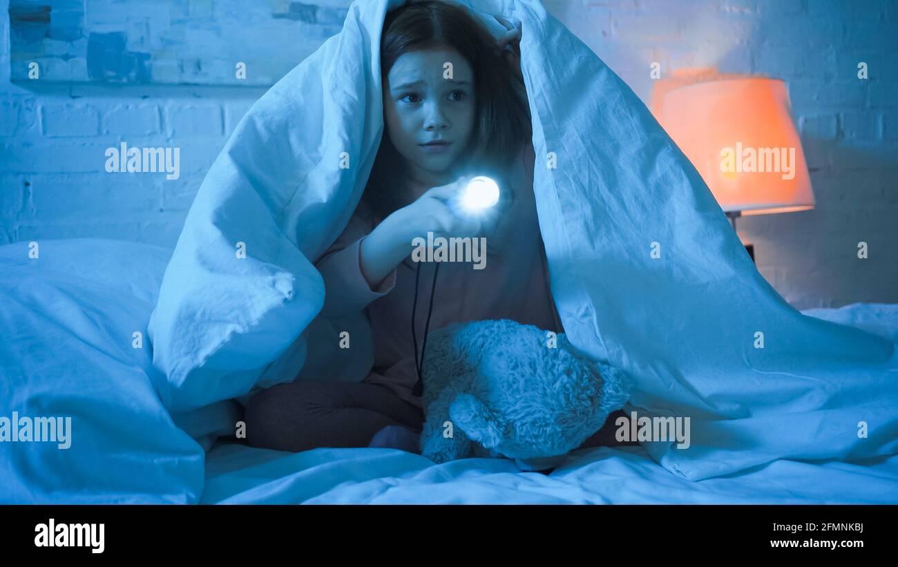 Girl holding flashlight near soft toy on bed in night Stock Photo - Alamy