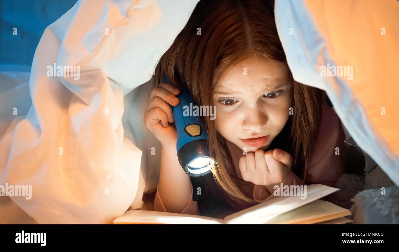 Concentrated kid with flashlight reading book on bed Stock Photo - Alamy