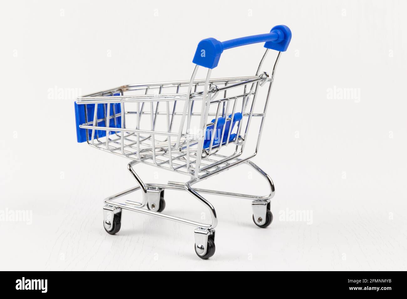 empty metal shiny grocery cart on wheels on white wooden table ...