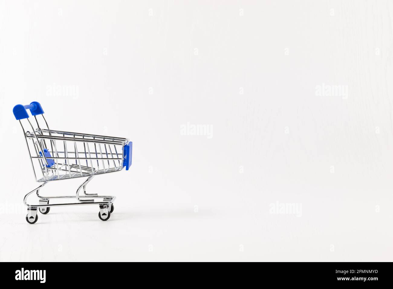 empty metal shiny grocery cart on wheels on white wooden table ...