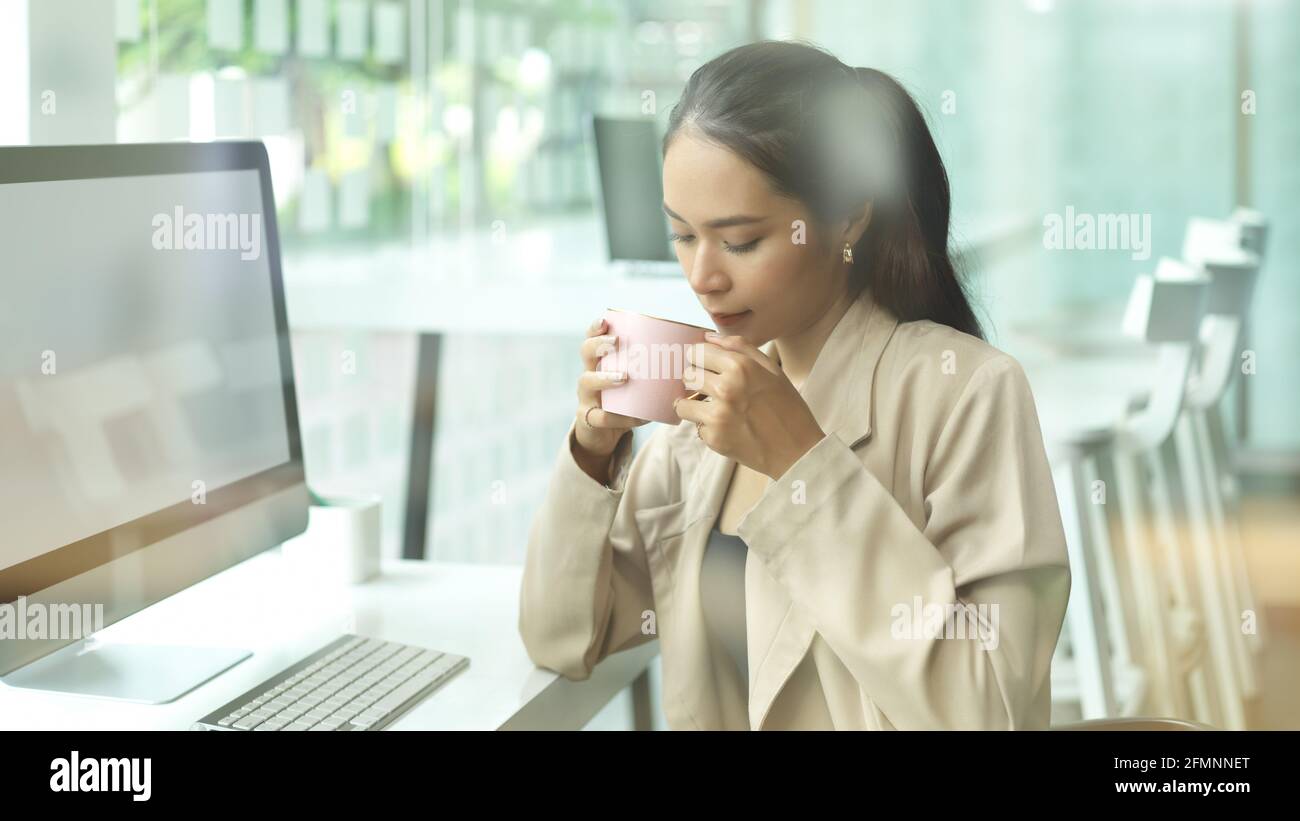 View through glass window of female office worker drinking coffee break ...
