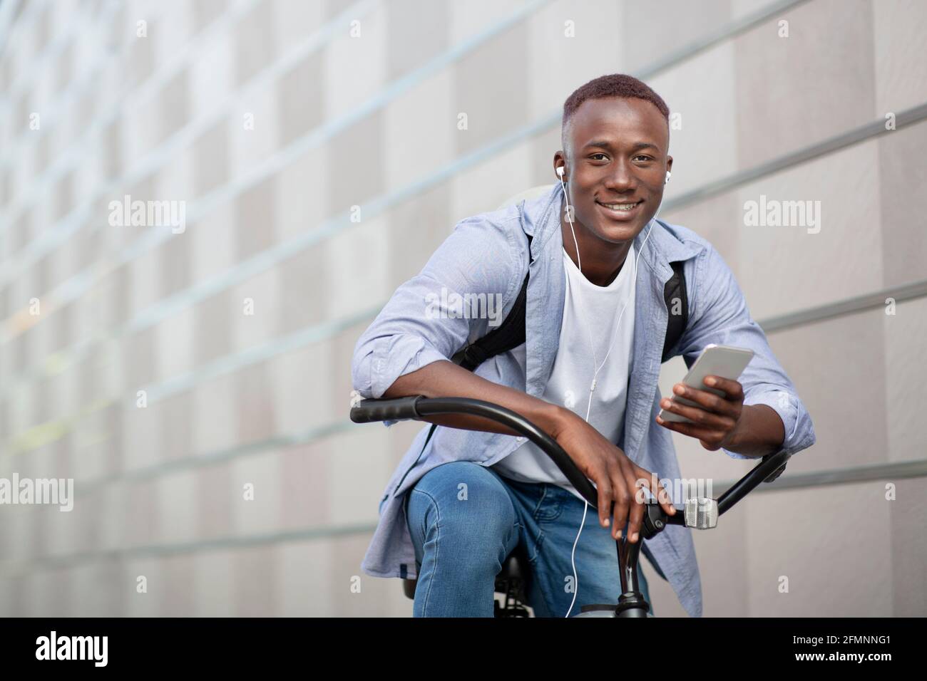 Handsome black guy with rucksack, earphones and mobile device riding ...
