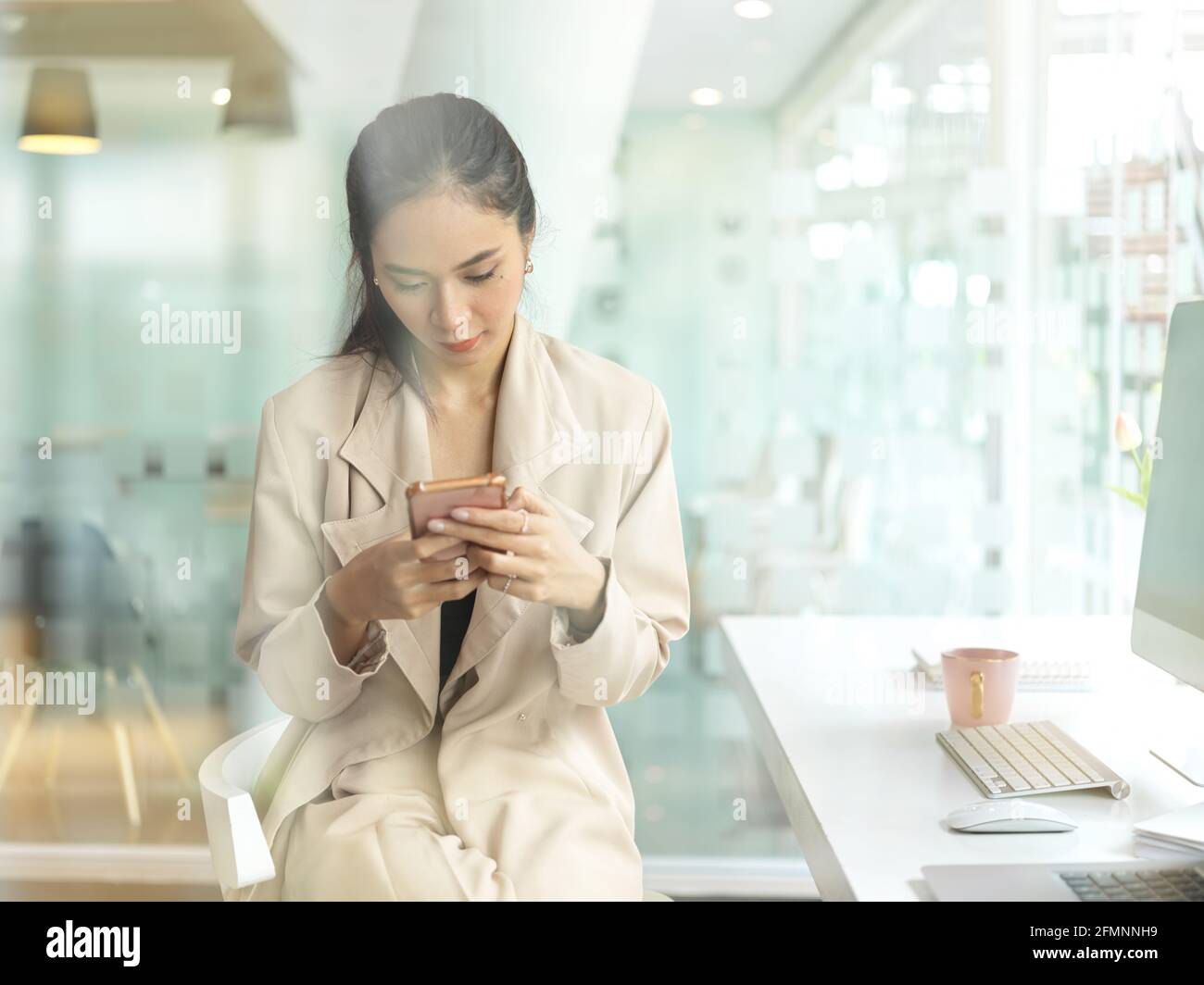 View through glass window of female office worker texting on smartphone ...