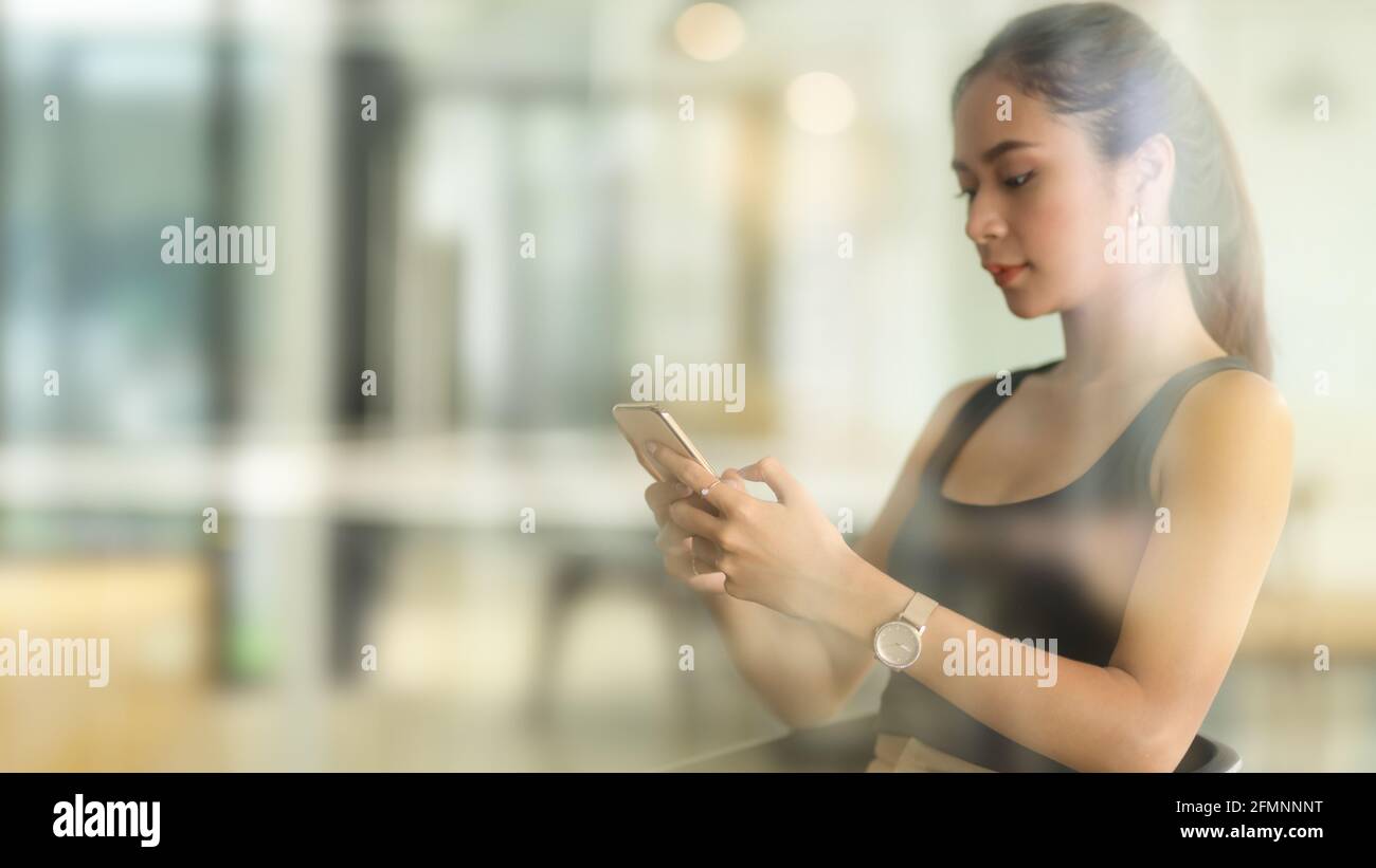 View through glass window of female entrepreneur texting on smartphone ...