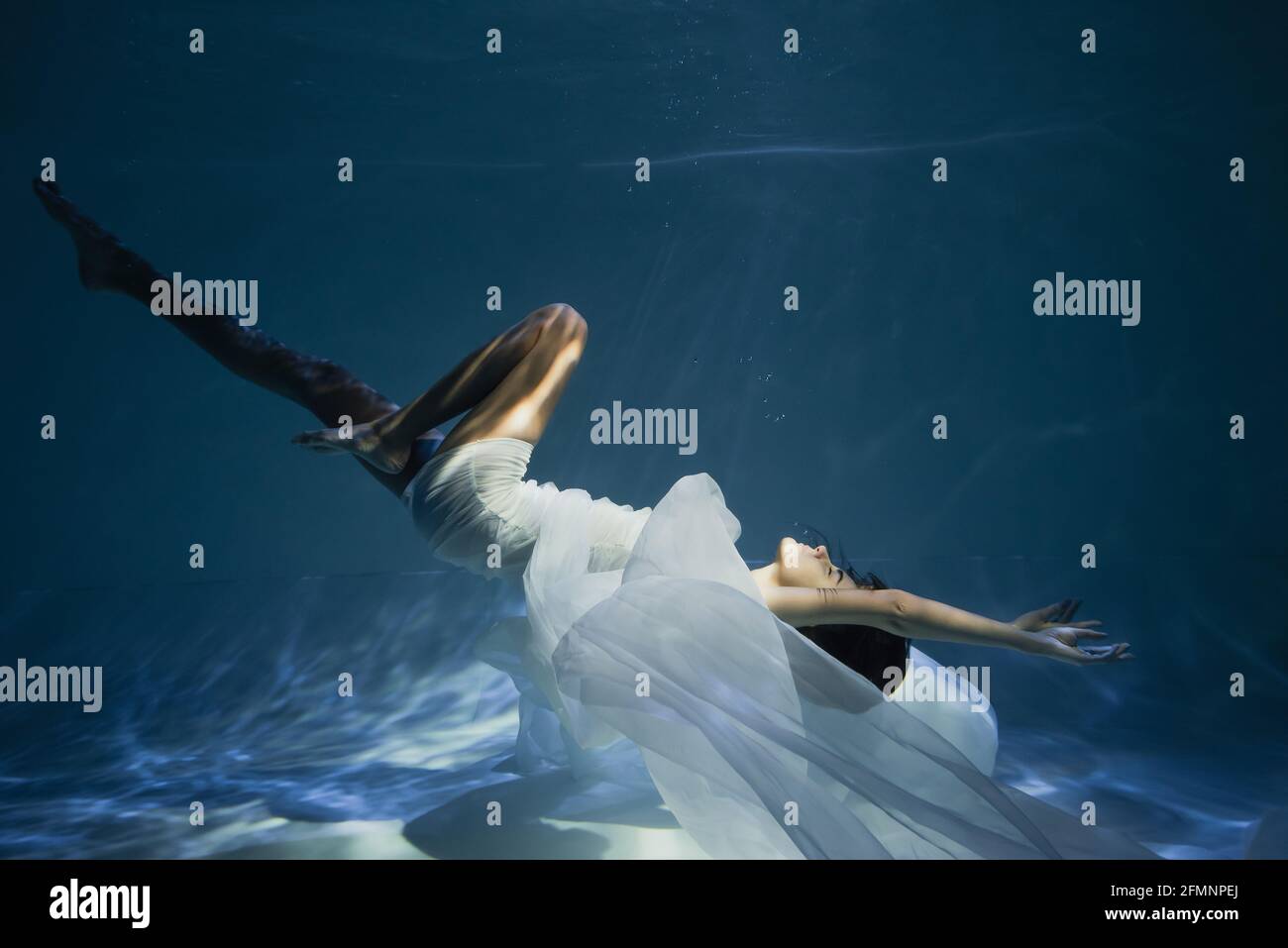 lighting on young woman in white dress diving in pool with blue water ...