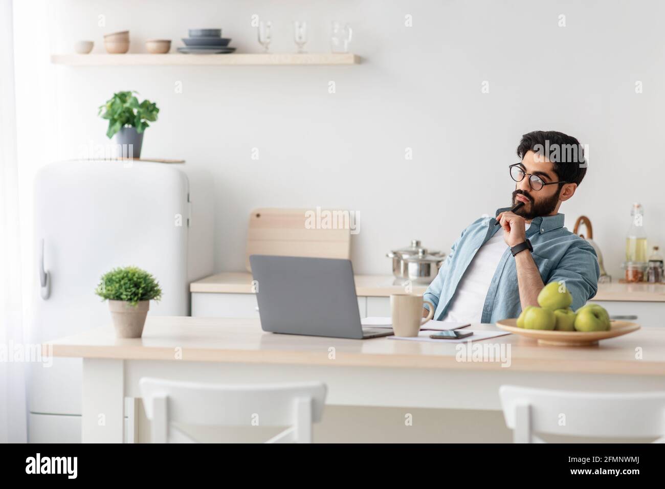 Remote work. Eastern freelancer working on laptop computer in kitchen interior at home, empty ...