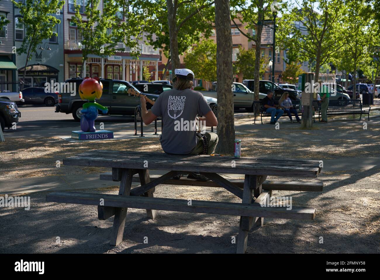 Man sitting on park bench playing banjo instrument, people sitting on ...