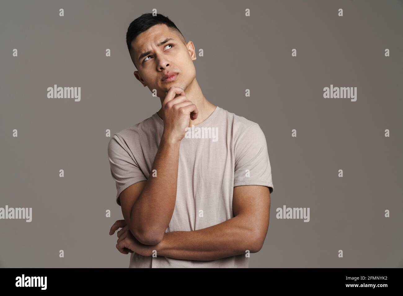 Puzzled handsome guy thinking and looking upward isolated over grey ...