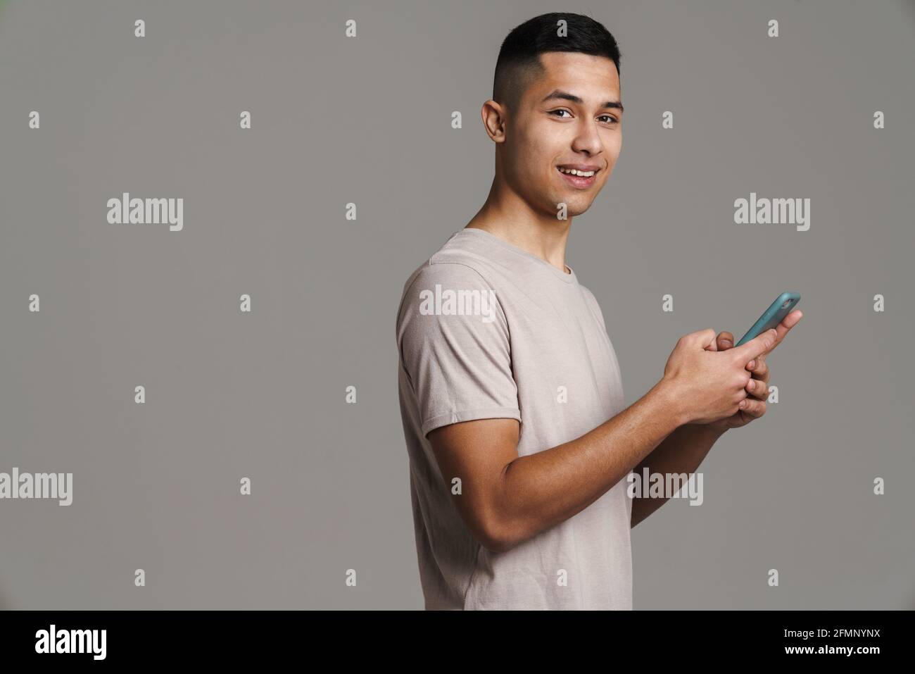 Happy handsome guy using mobile phone and smiling isolated over grey ...