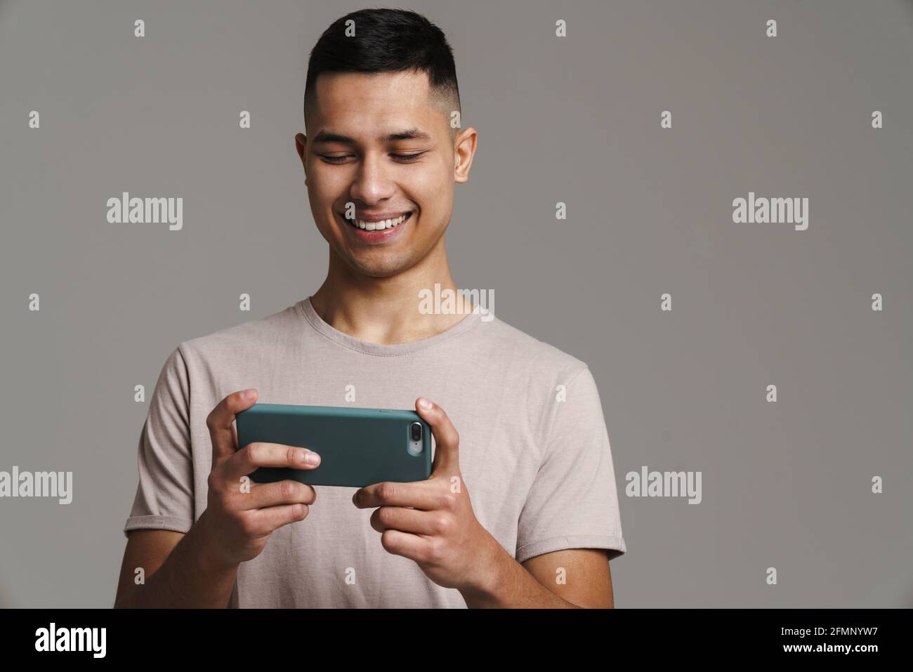 Happy handsome guy using mobile phone and smiling isolated over grey ...