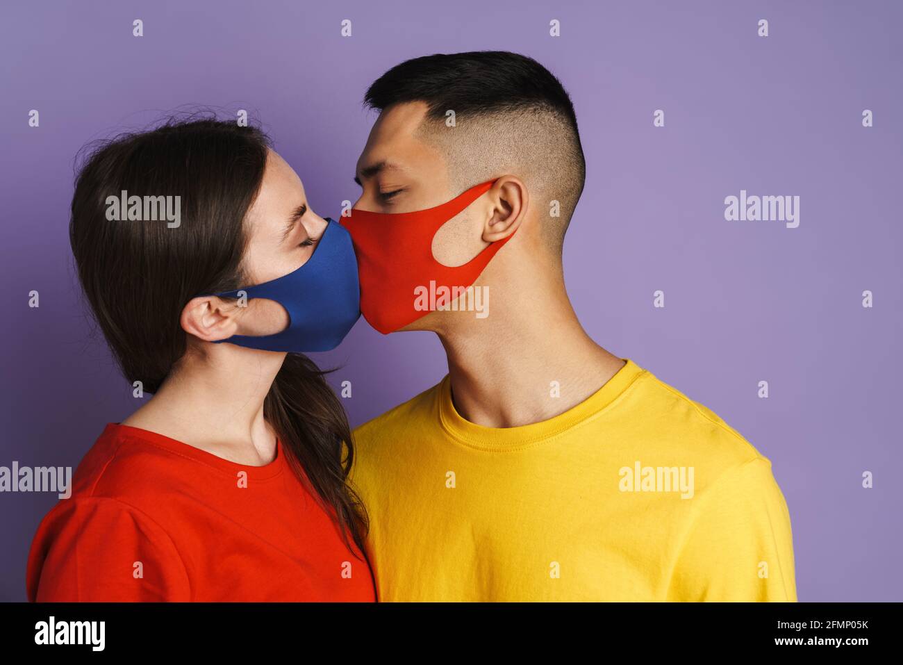 Brunette young couple in face mask kissing at camera isolated over ...