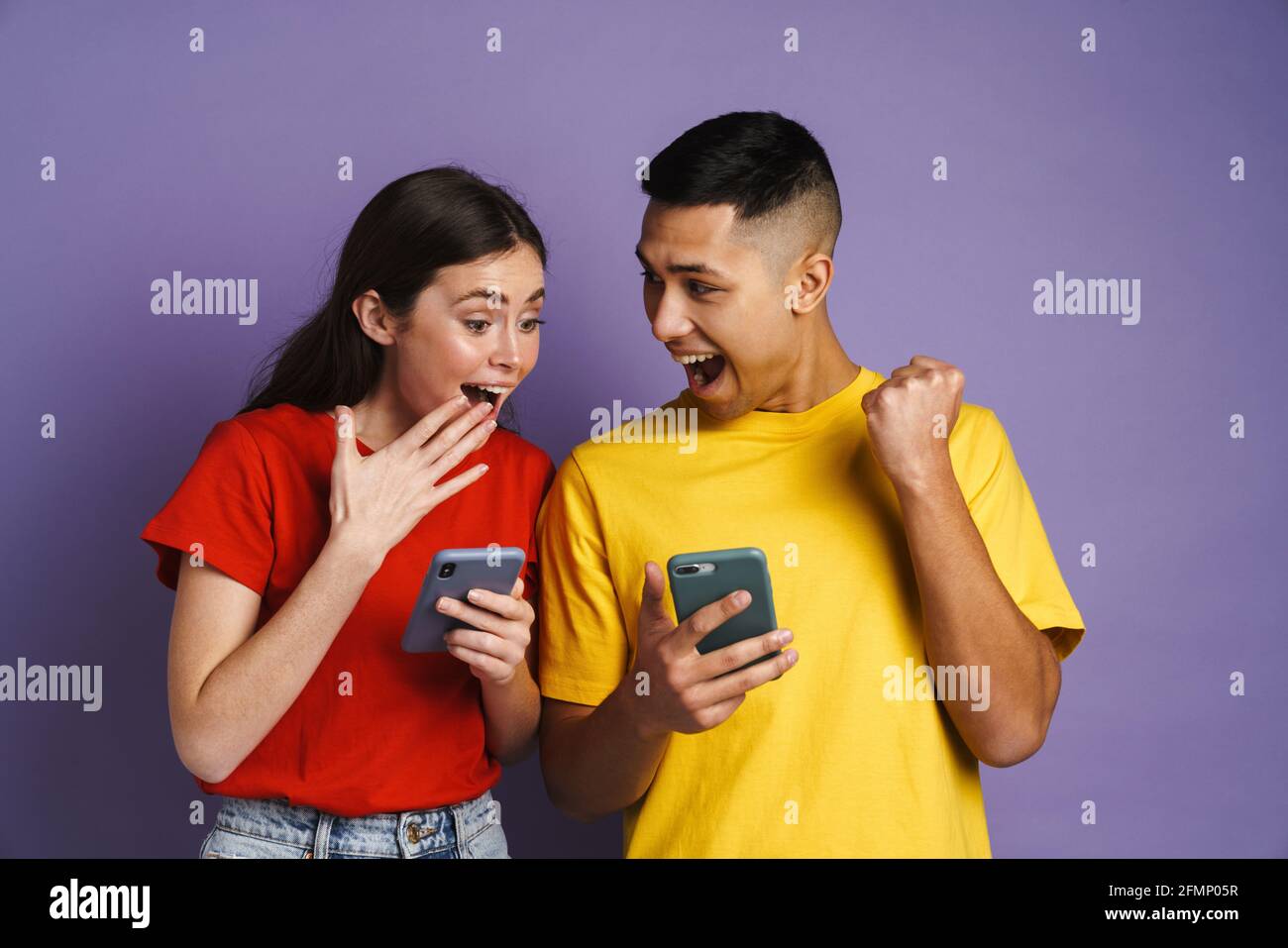 Excited couple making winner gesture while using mobile phones isolated ...