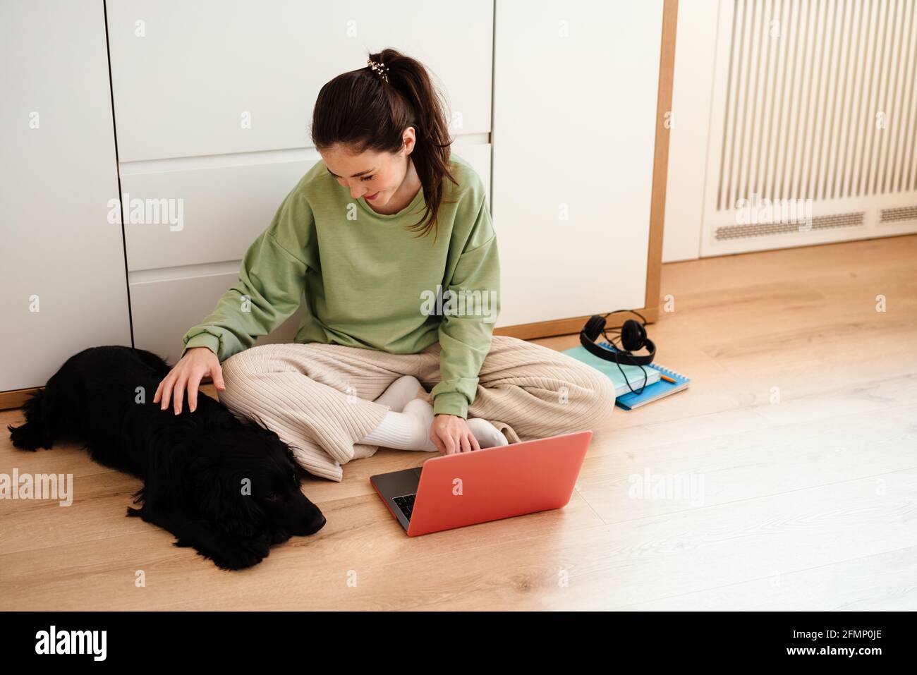 Happy brunette young woman petting her dog while studying at home ...