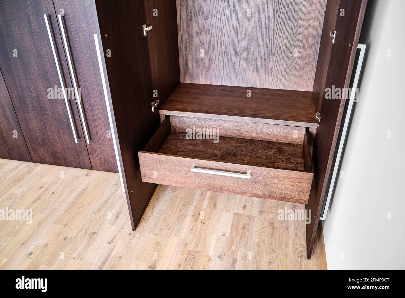 Open doors and drawer of elegant wardrobe made of dark oak veneer with ...