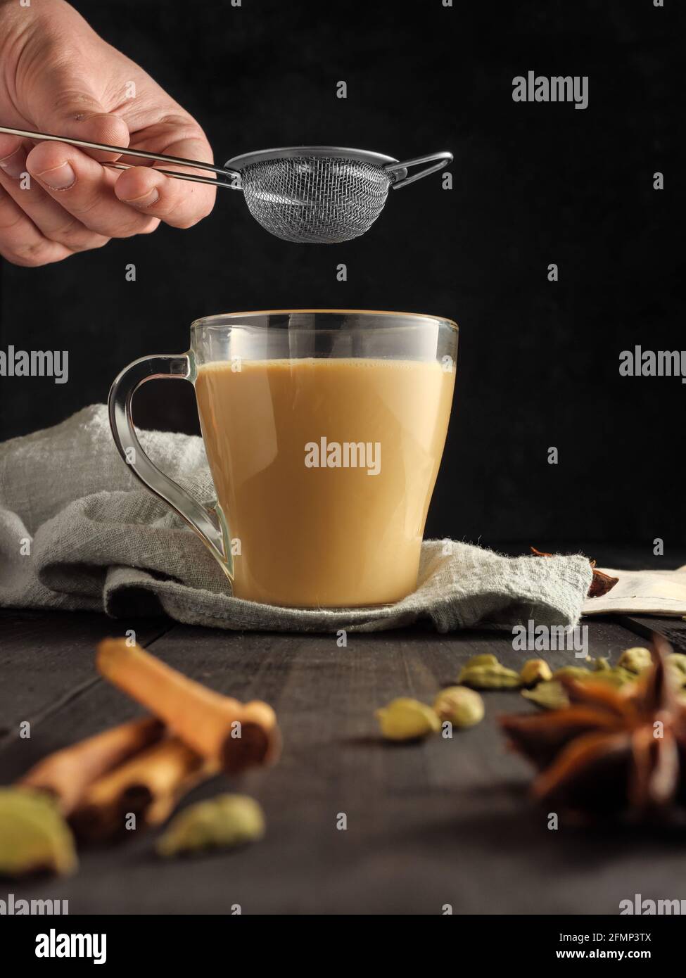 A male hand holds a sieve for straining masala tea over a glass mug ...
