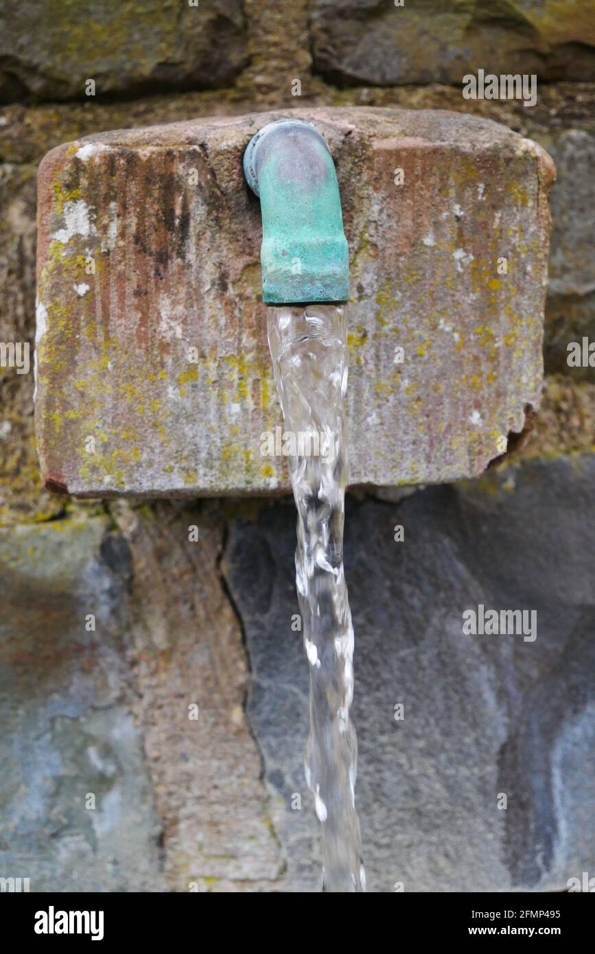 closeup of a green faucet with running water from an old stone block of ...