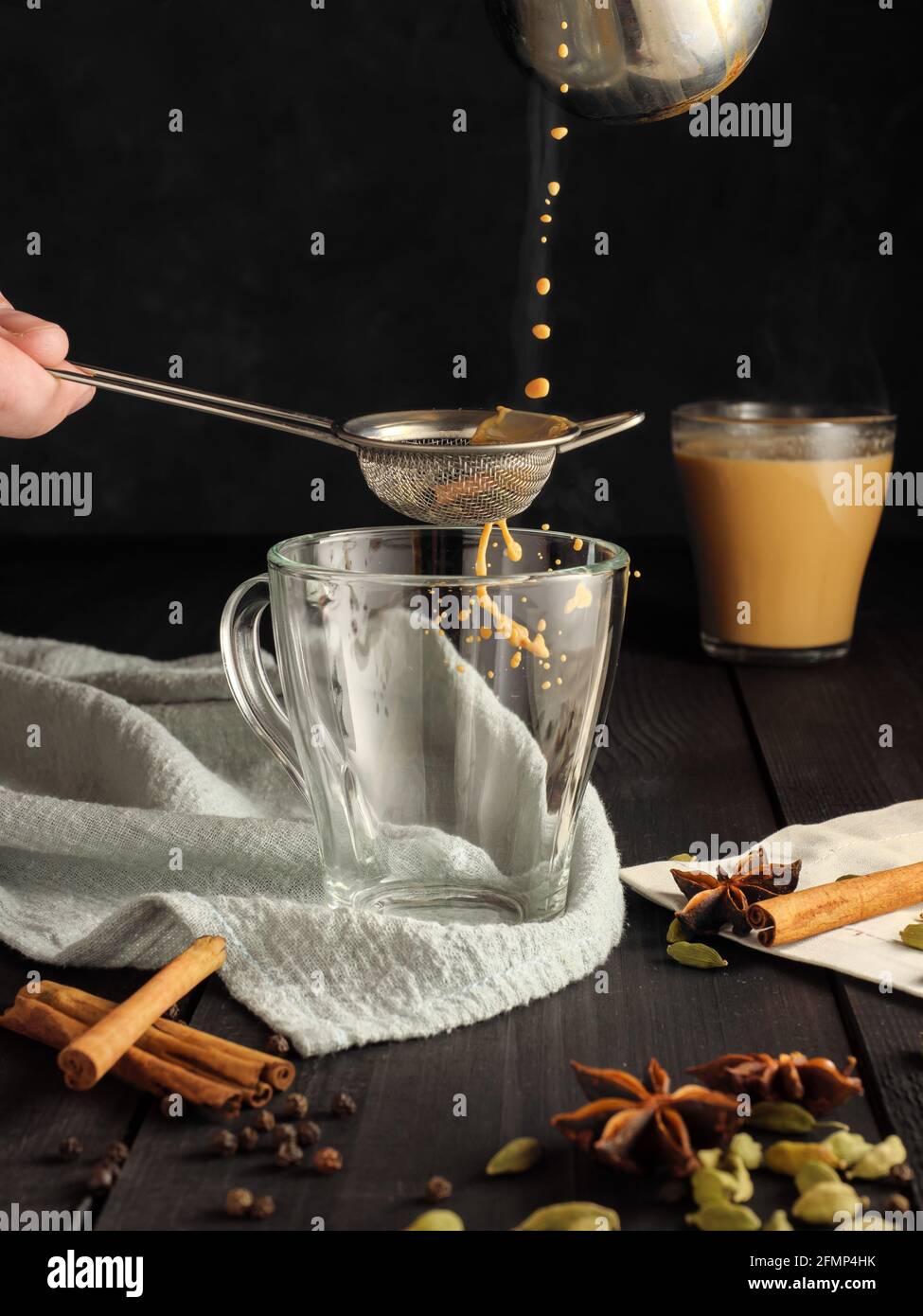 Masala tea is poured through a sieve into a glass mug. Species are on ...